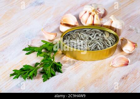 Image of pickled eels in open tin can with garlic at table, nobody ...