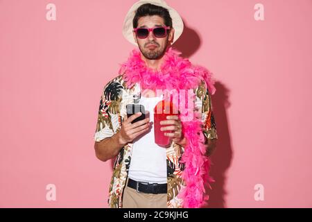 Portrait of unhappy man wearing boa using cellphone while drinking soda ...
