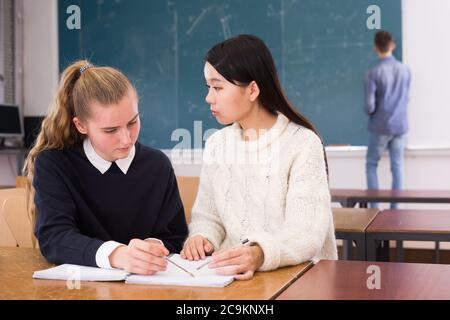 Intelligent girl student helping her Chinese girl schoolmate prepare ...