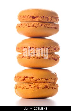 Three orange flavoured macaroons standing on top of each other on white ...