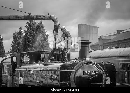 Steam train crew fireman filling water tank of vintage steam locomotive ...