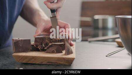 man hands breaking big dark chocolate block with knife on wood board ...