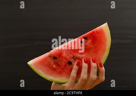 Semicircle of ripe watermelon in female hands on a black background ...