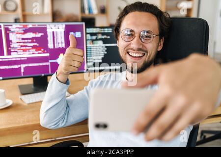 Image of joyful man showing thumb up and using cellphone while playing ...