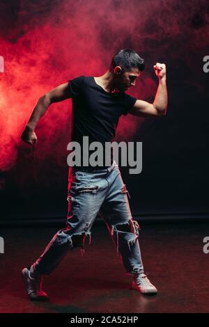 young vigorous male dancing isolated over red smoky space, wearing ...