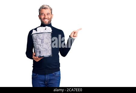 Young caucasian man holding wastebasket with recycling plastic bottles ...