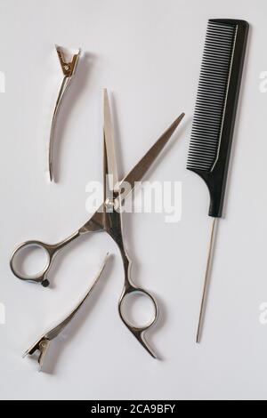 Closeup of metal hair clips, a comb, and scissors on a black background ...