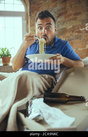 Shocked eating instant noodle. Lazy man living in his bed surrounded ...