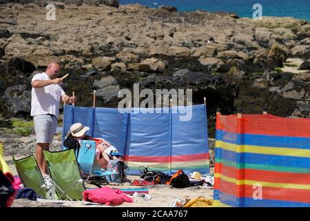 Man erecting wind break on beach. Standing with mallett over posts Blue ...