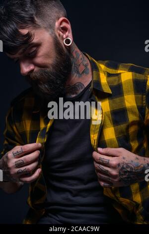 Close-up of bearded man with tattoos listening to audio in earphones ...