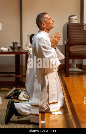 Wearing a white robe, a deacon prays on his knees in the chapel of a ...