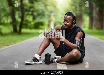 African jogger drinking water and using smartphone Stock Photo - Alamy