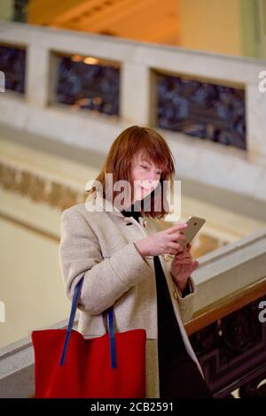 A woman looks at her mobile phone while standing Stock Photo - Alamy