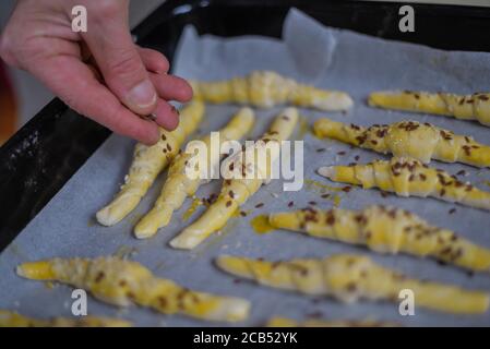 Closeup shot of a person pouring seed toppings onto rolled up pastries ...