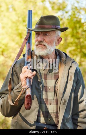Older hunter man with grey beard holding gun to hunt on birds, ready to ...