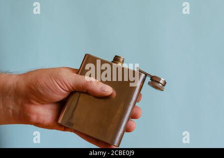 Hand holds metal hip flask. Left male hand with an open small flask ...