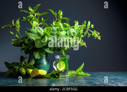 Mint tea with lime slices and bunch of fresh mint on a dark background ...