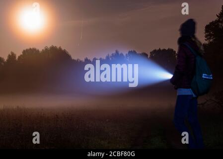 A person with a flashlight on a foggy meadow, with a flashlight in the ...