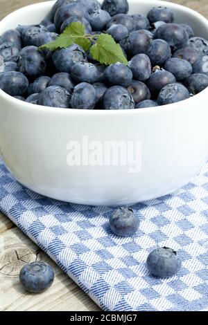 Fresh blueberries in white ceramic bowl on light stone surface with ...