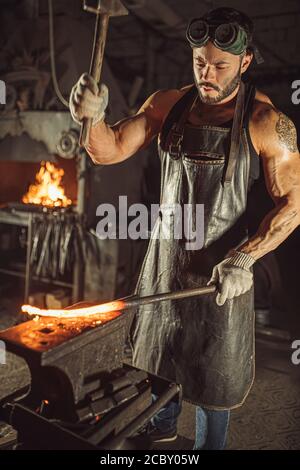 strong muscular brutal confident blacksmith man shaping red hot metal ...