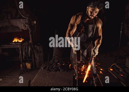 young muscular blacksmith man manually forging the molten metal ...