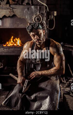 young strong muscular blacksmith wearing black apron and gloves for ...