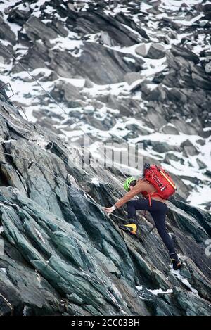 Side view alpinist with backpack using fixed rope to climb high rocky ...