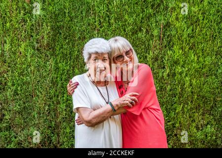 Positive senior female in casual clothes resting after watering plants ...