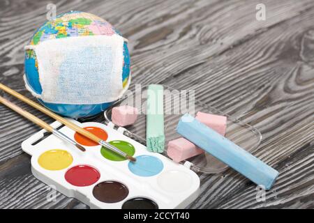 Globe with medical mask. Nearby watercolors, crayons and pencils ...