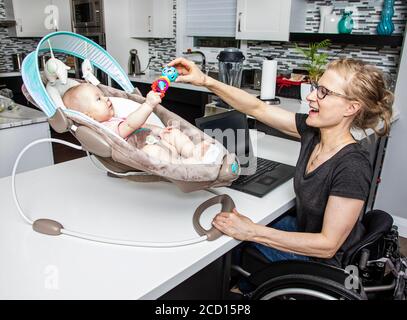 A paraplegic mother playing with her baby in a play pen and holding her ...