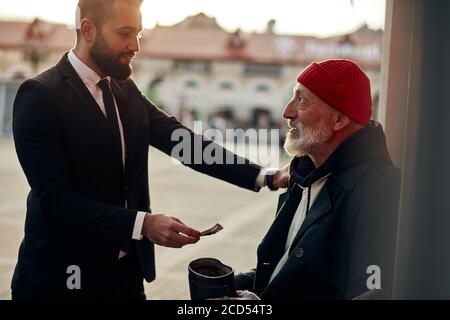 Businessman in tuxedo help to vagrant man sitting on street with rusty ...