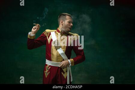Disguasted smoking cigarette. Young man in suit as Nicholas II on dark ...