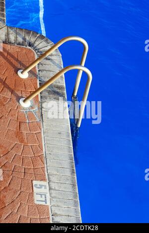 Swimming pool ladder at deep end separated from shallow pool by ledge ...
