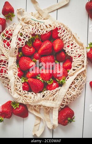 Ripe eco strawberries in a wooden plate on a background of palm leaves ...