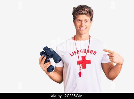 Young handsome man wearing lifeguard uniform holding float pointing ...