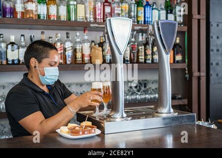 Ethnic female in mask pouring sanitizer on hands while riding on ...