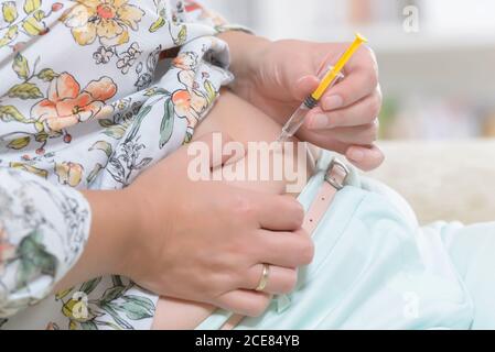 Woman is doing an insulin or heparin injection in her abdomen at home ...