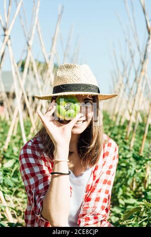 Charming young woman gardener in overalls view through lush foliage ...