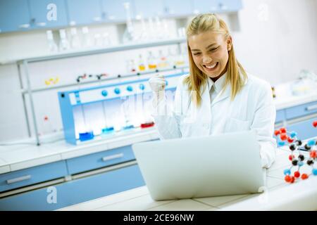 Cute happy female researcher in white lab coat using laptop while ...