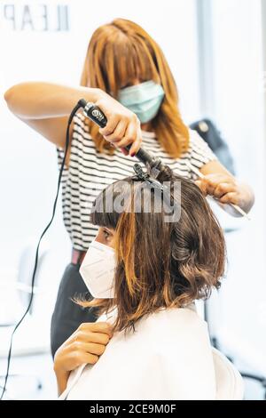 Hairdresser with mask and client, finishing the curly hairstyle ...