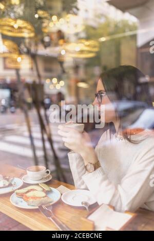 woman behind window in cafe. young girl in black dress sits at table ...