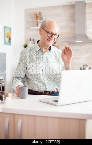 Old man saying hello during video call with family using notebook in ...