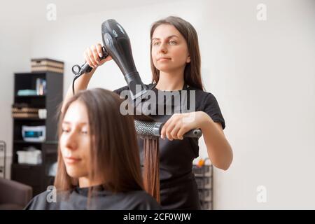 A hairdresser is drying long brown hair with a hairdryer and round ...