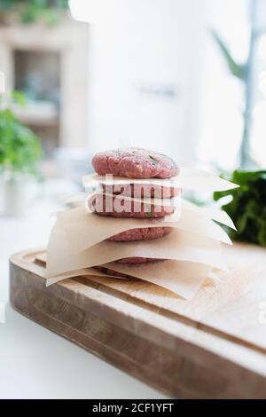Stack of raw hamburger meat patties on a wood table with pieces of ...