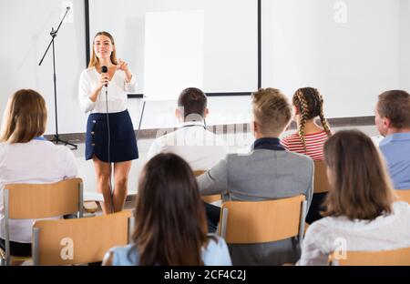 Confident female student answering with microphone in front of student ...