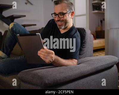 Relaxed man talking on the tablet smiling alone on the sofa in the ...