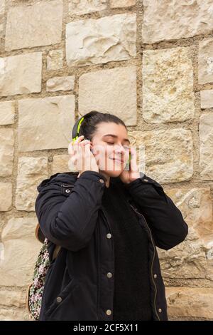 Satisfied young lady smiling while listening to music in earphones ...
