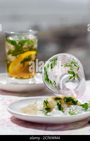 Iced tea with frozen water cubes spilled on saucer with lemon and mint ...