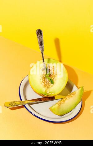 Cut ripe appetizing sweet pitted melon on plate with spoon and fork in ...