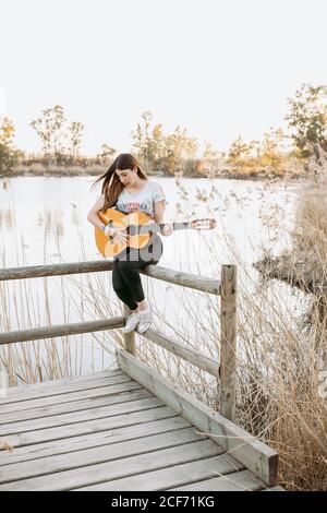 Calm lady looking at the guitar while playing it at the sports ground ...